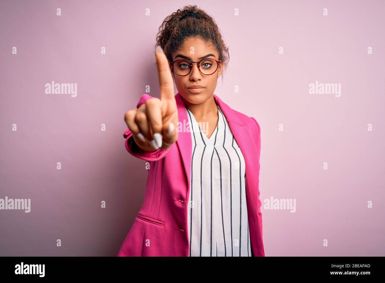Beautiful african american businesswoman wearing jacket and glasses over pink background ...