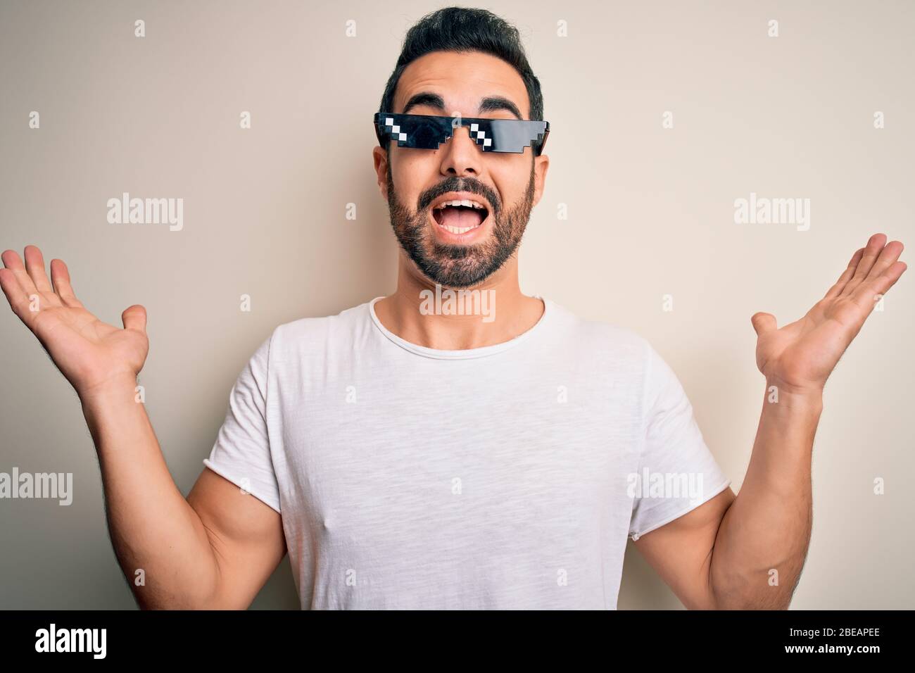 Young handsome man with beard wearing funny thug life sunglasses over ...