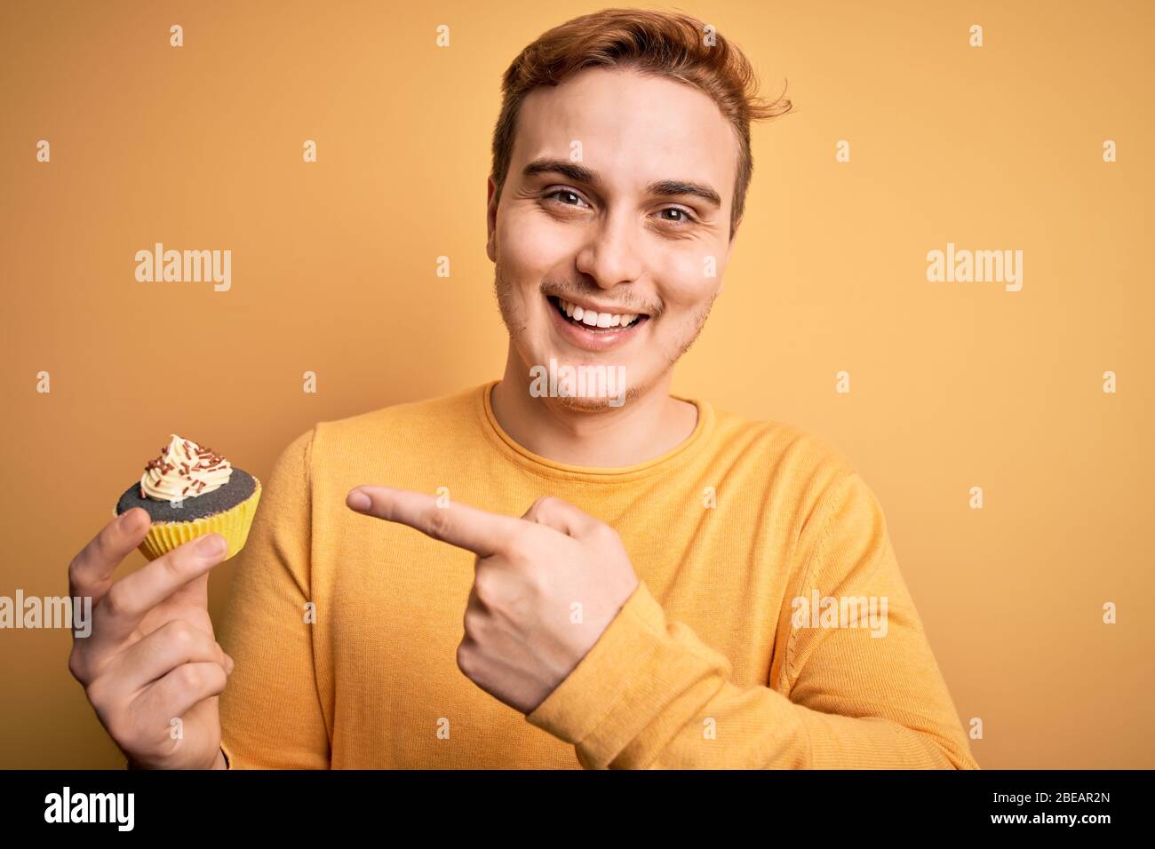 Young handsome redhead man eating sweet chocolate cupcake dessert over ...