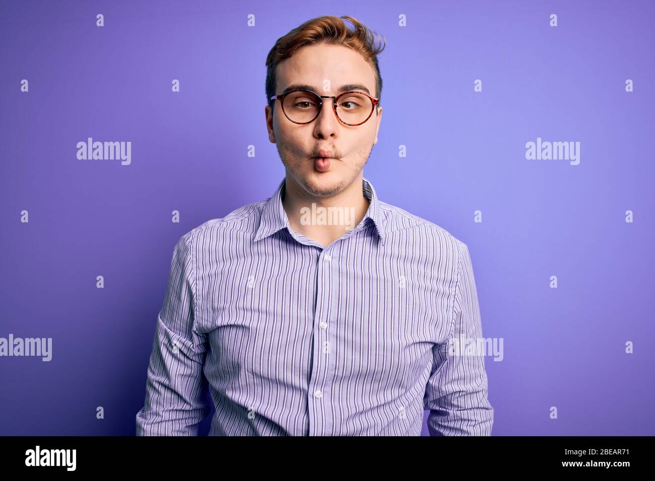 Young handsome redhead man wearing casual shirt and glasses over purple ...