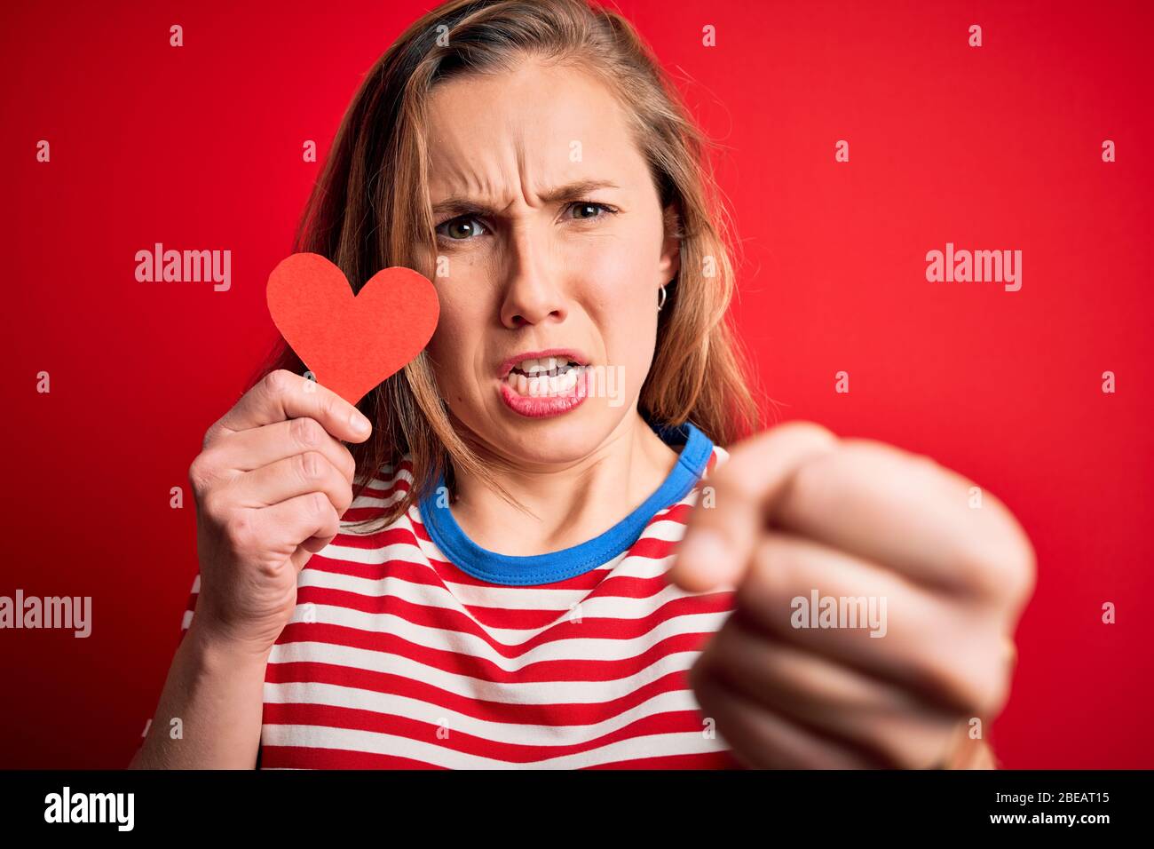 Young beautiful blonde woman holding paper heart standing over isolated ...