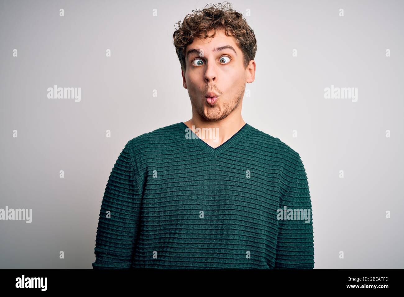 Young blond handsome man with curly hair wearing green sweater over ...