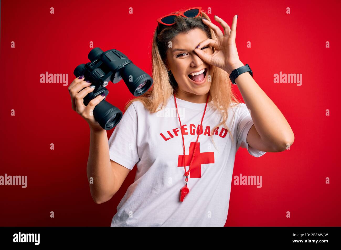 Young beautiful blonde lifeguard woman using binoculars and whistle ...