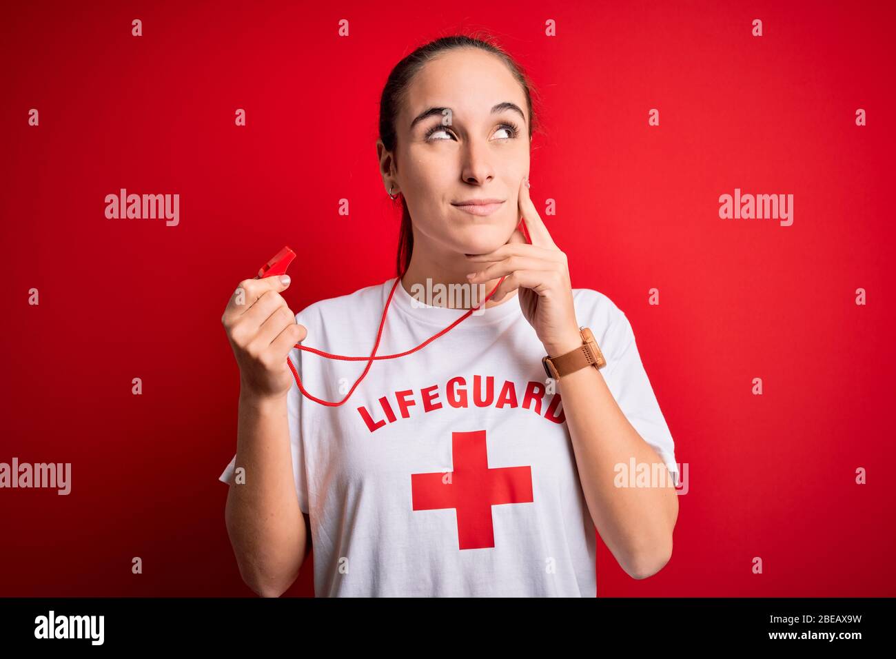 Beautiful lifeguard woman wearing t-shirt with red cross using whistle ...