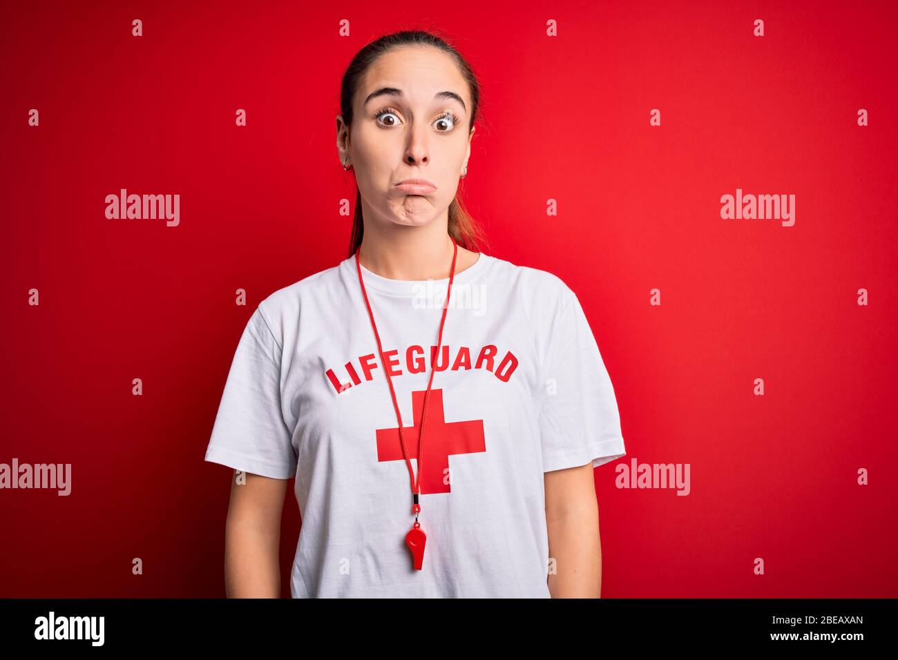 Beautiful lifeguard woman wearing t-shirt with red cross using whistle ...