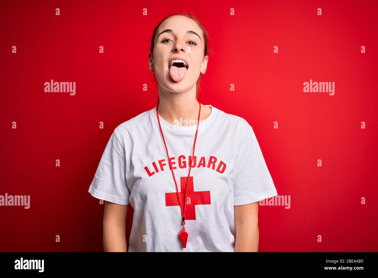 Beautiful lifeguard woman wearing t-shirt with red cross using whistle ...