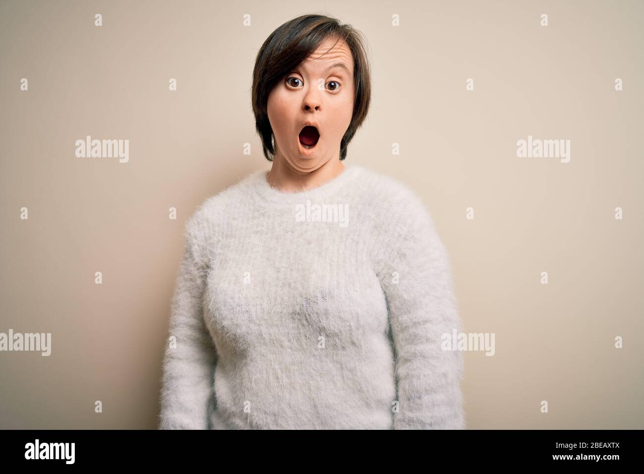 Young down syndrome woman standing over isolated background afraid and ...