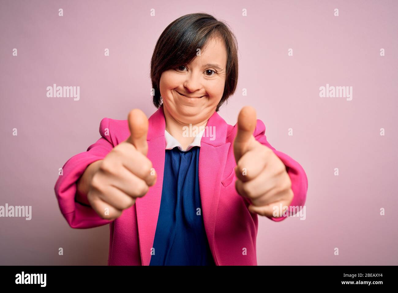 Young down syndrome business woman over pink background approving doing ...