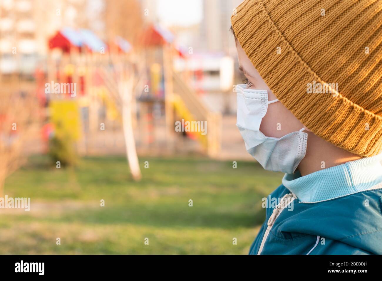 A boy in a protective mask stands near a playground in the street ...