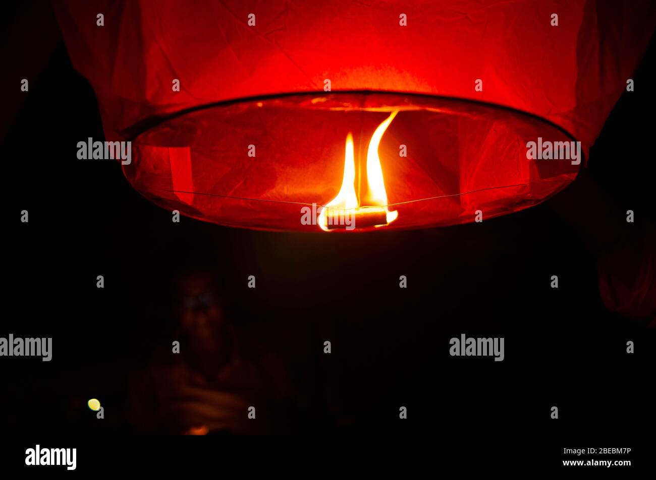 A red coloured sky lantern with the flames showing clearly lifiting off ...