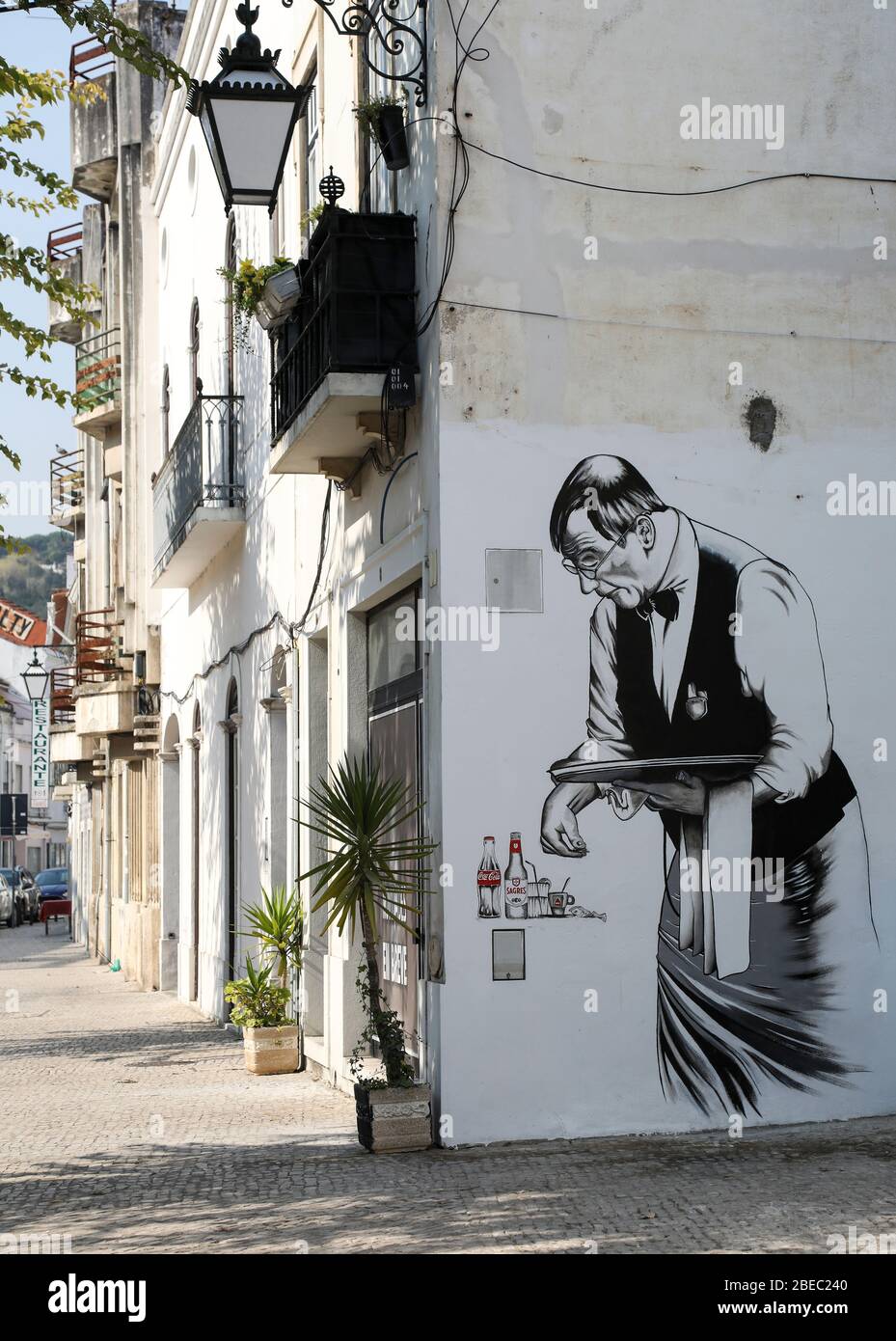 A mural of a waiter seen on the side of a white traditional building of ...