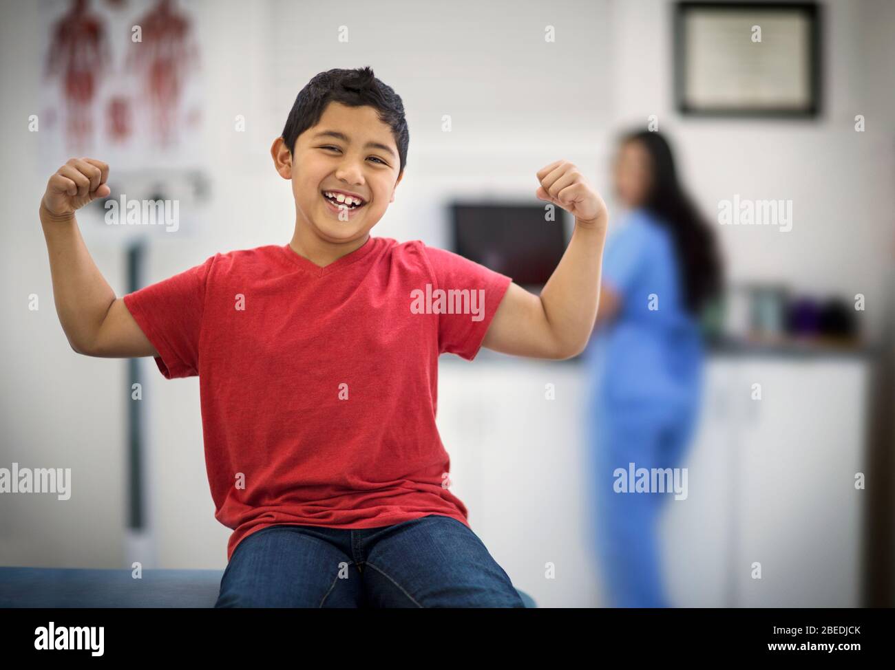 Portrait of a laughing young boy flexing his muscles while sitting ...
