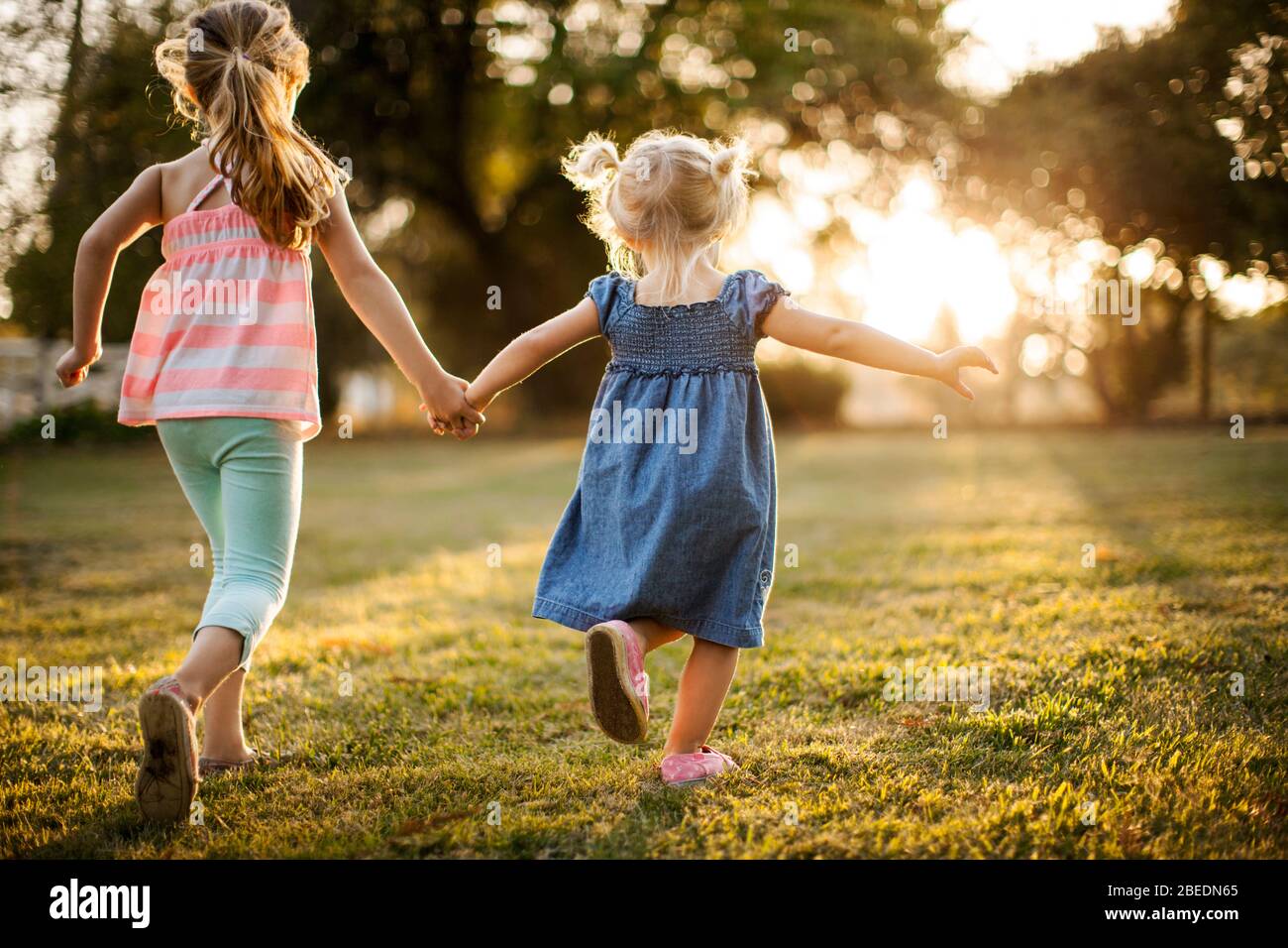 Two young girls running hand in hand through a park Stock Photo - Alamy