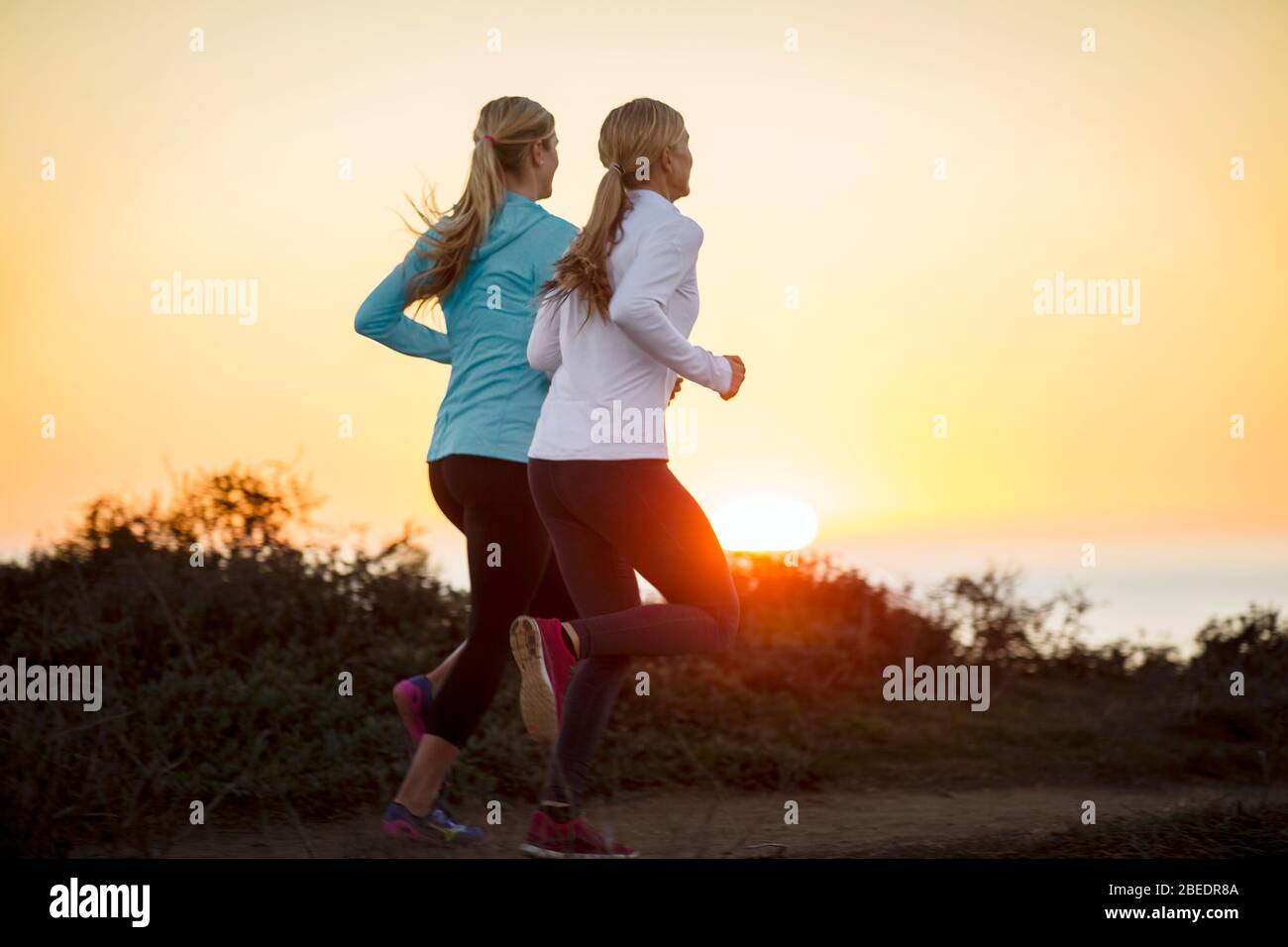 Two young women jogging together along the cliffs by the ocean at ...
