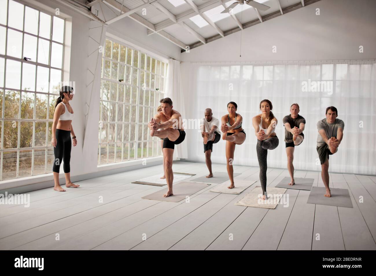 A group of people in a yoga class standing on one leg with their ...