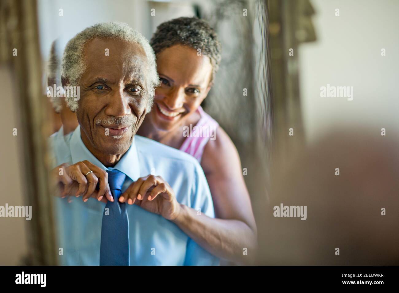 Mid adult woman helping her father with his tie while looking in the ...
