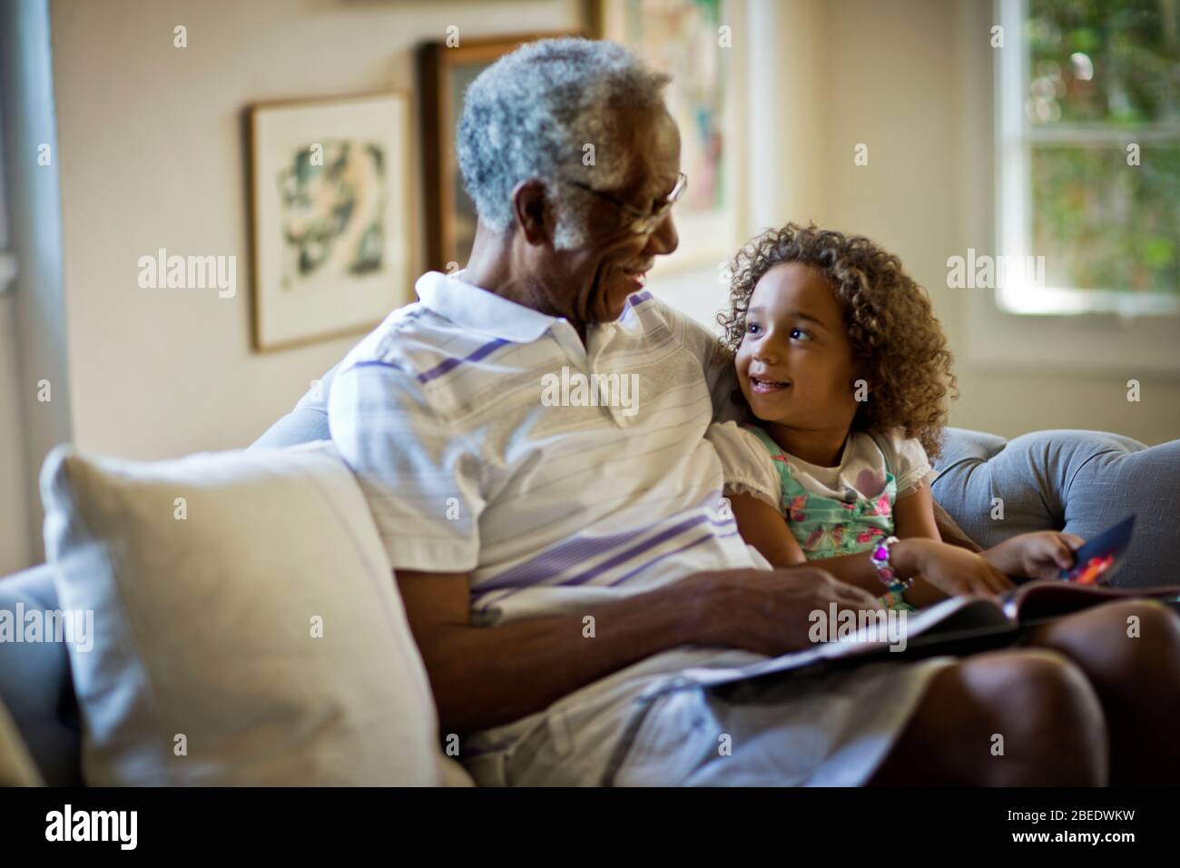 Happy Senior Man Reading A Storybook With His Young Granddaughter Stock