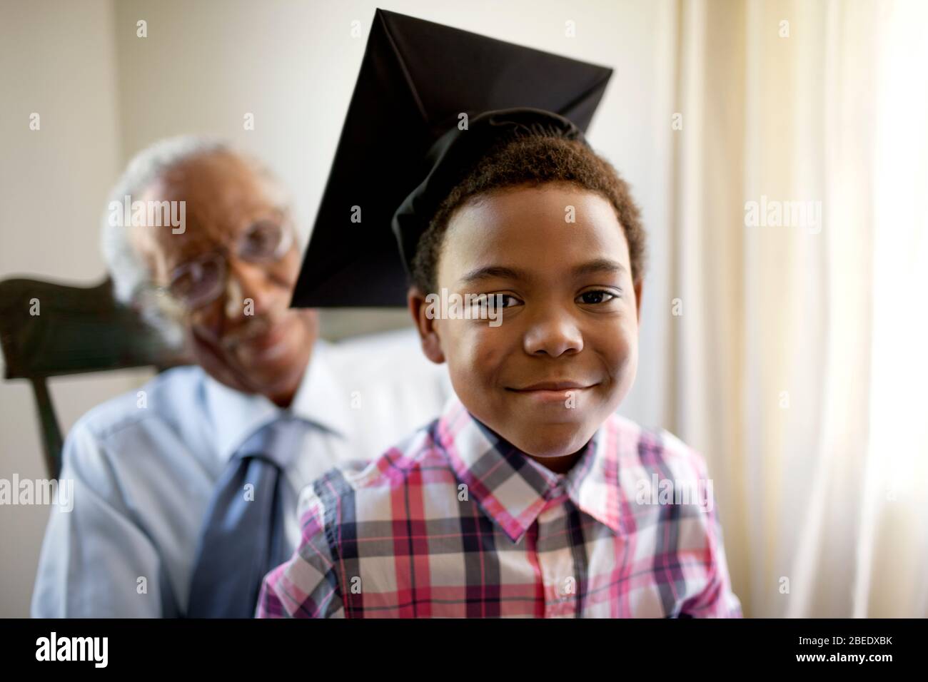 Portrait of young boy with graduation cap sitting with his grandfather ...