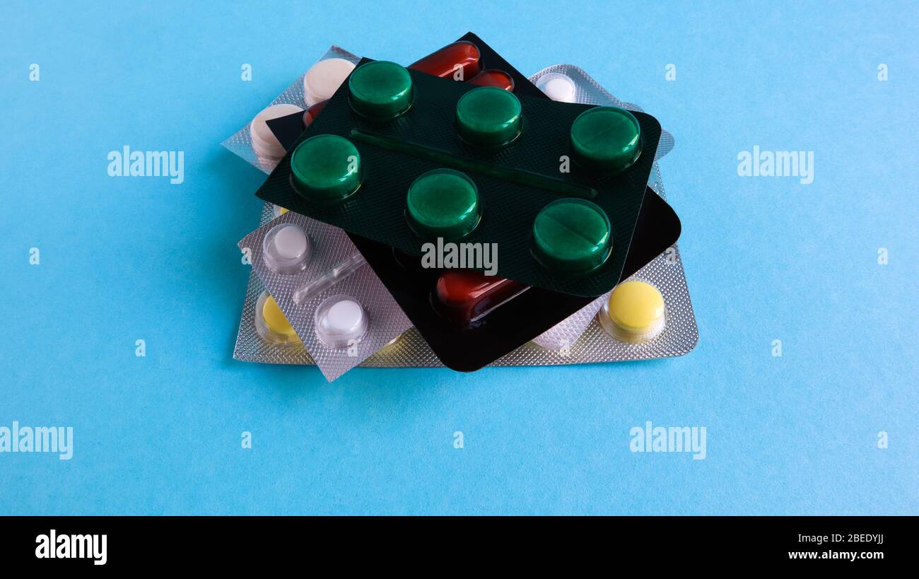 Packs of pills of various shapes and colors are stacked on a blue ...