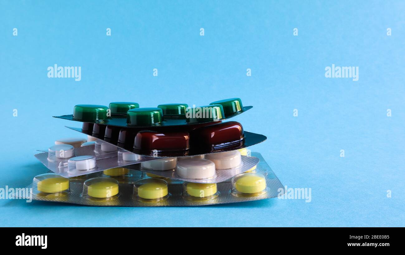 Packs of pills of various shapes and colors are stacked on a blue ...