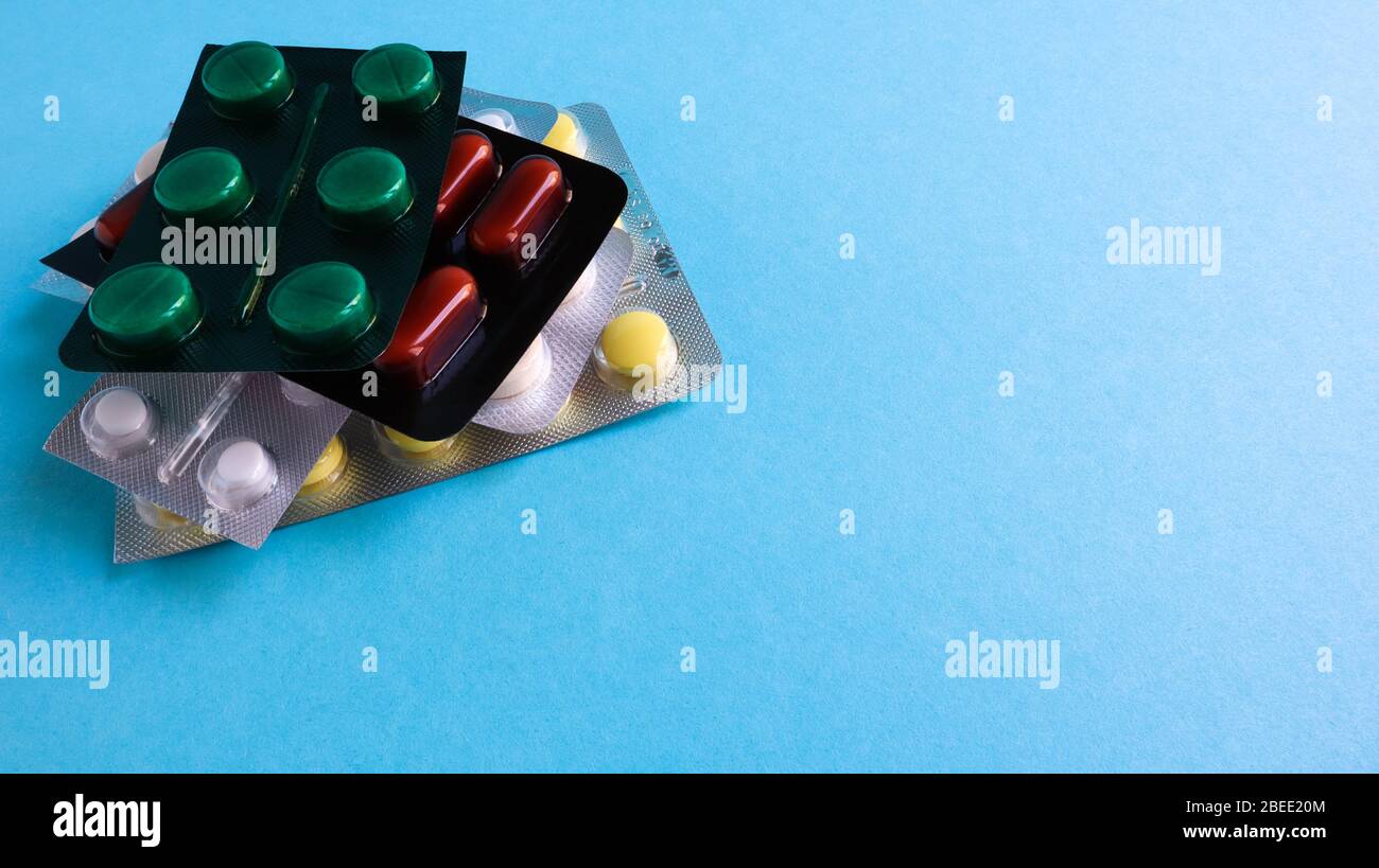 Packs of pills of various shapes and colors are stacked on a blue ...