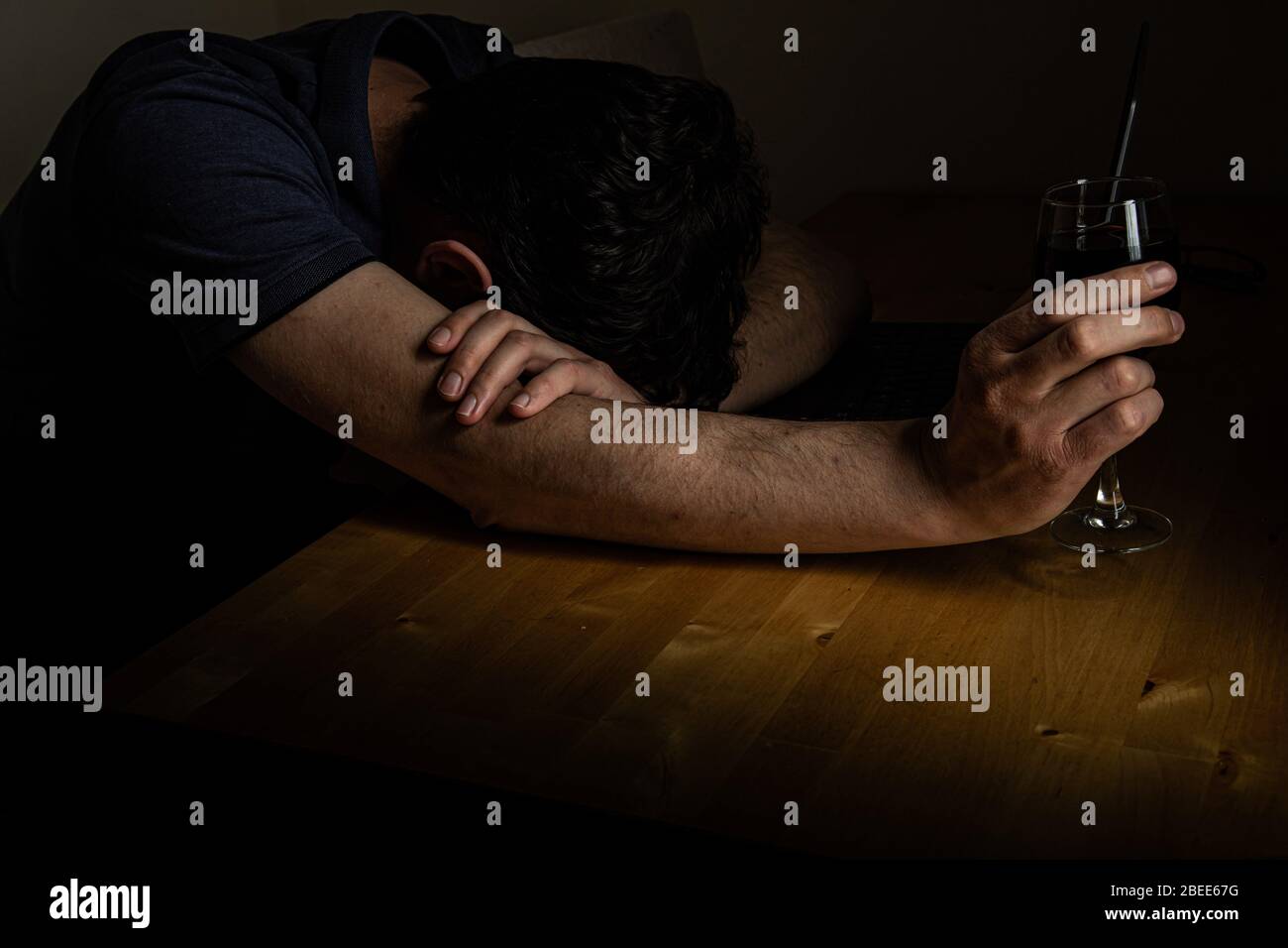 Drunk man leaning on the table near laptop and holding wineglass ...