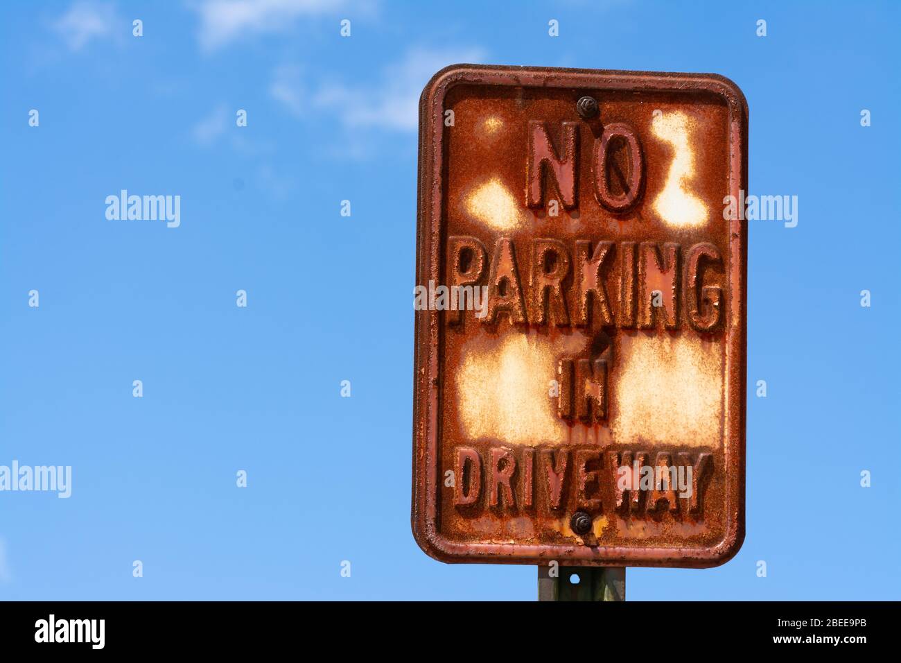 Rusted No Parking In Driveway street sign with blue skies in the ...