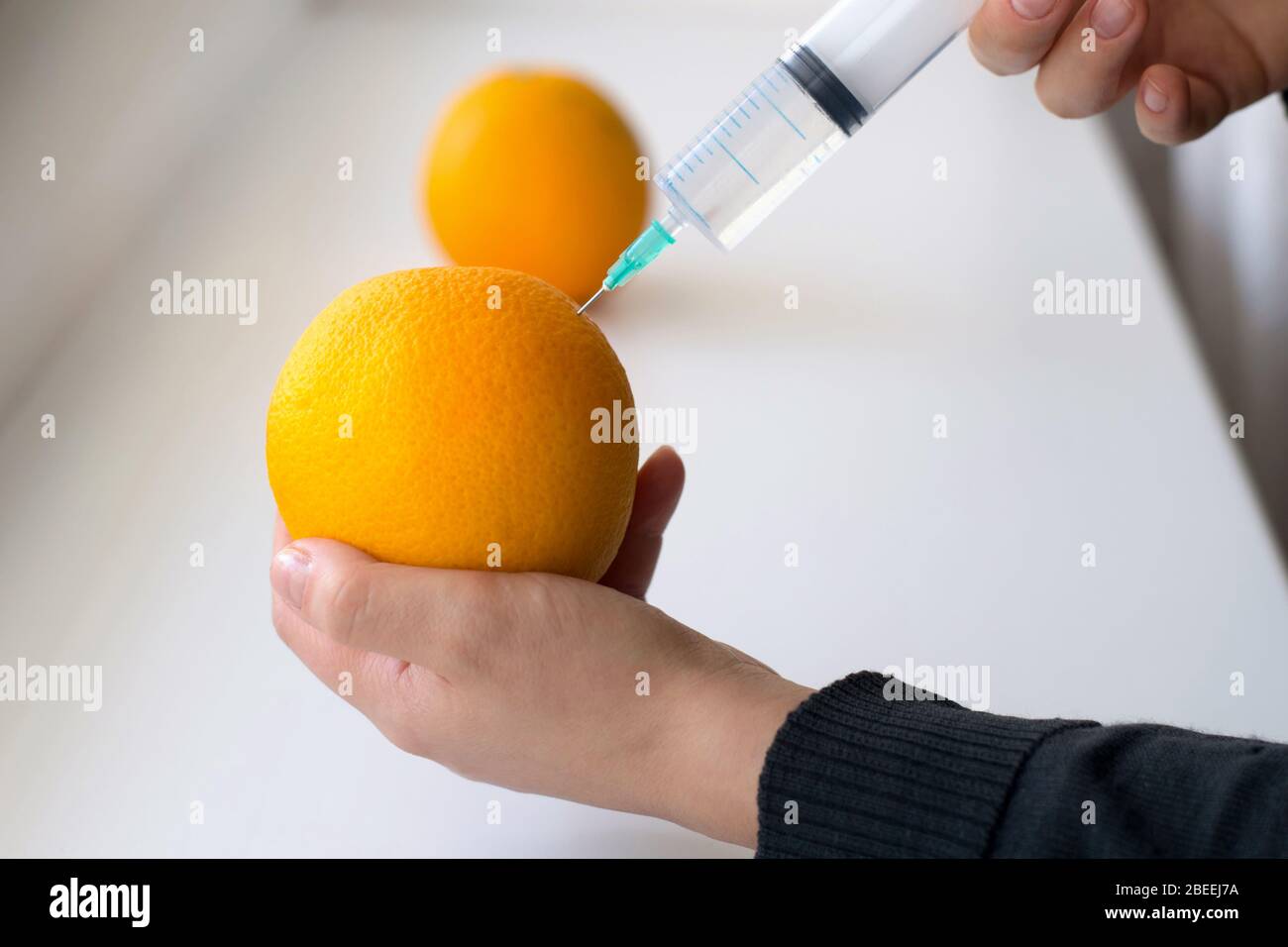 Photo of hand making injection into an orange on a light background ...