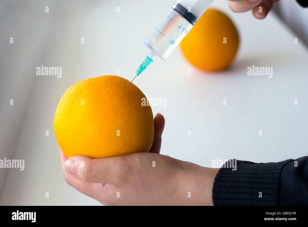 Photo of hand making injection into an orange on a light background ...