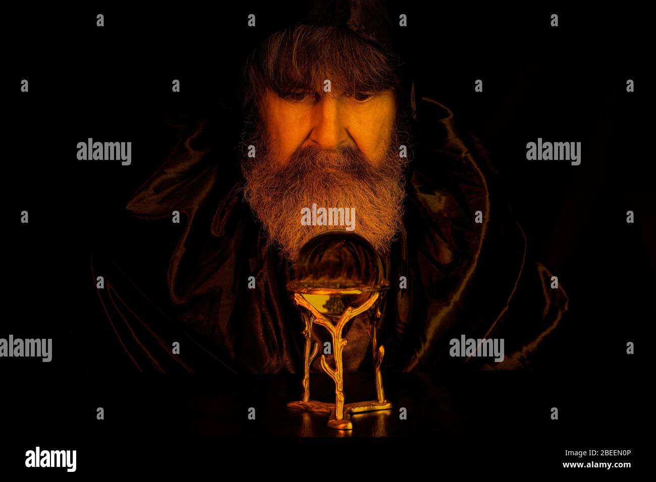 Wizard gazing into a crystal ball. He wears a dark cloak. Shallow depth ...