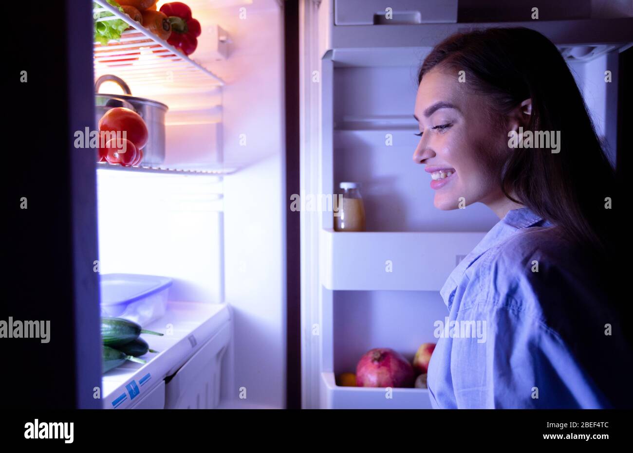 Cheerful girl looking for food in fridge late in night Stock Photo - Alamy