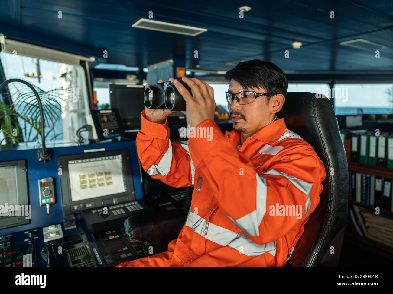 Filipino deck Officer on bridge of vessel or ship looking through ...