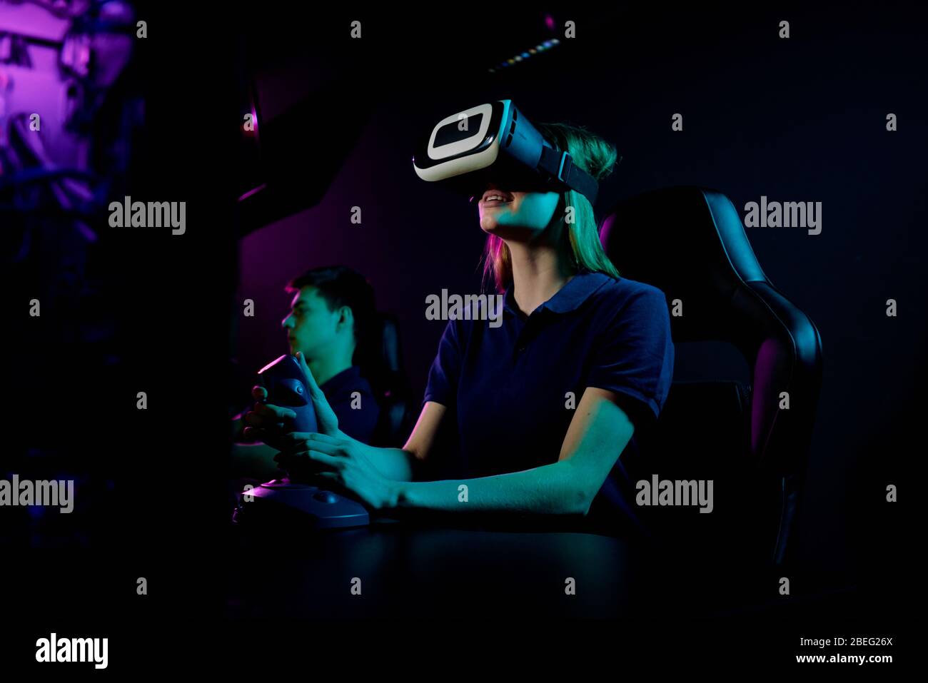 Smiling girl in virtual reality goggles sitting in gamers armchair and ...