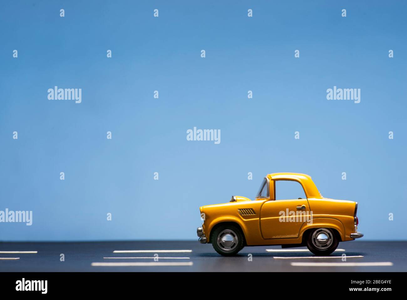Side view of a Yellow toy car on a blue background and on an asphalt ...