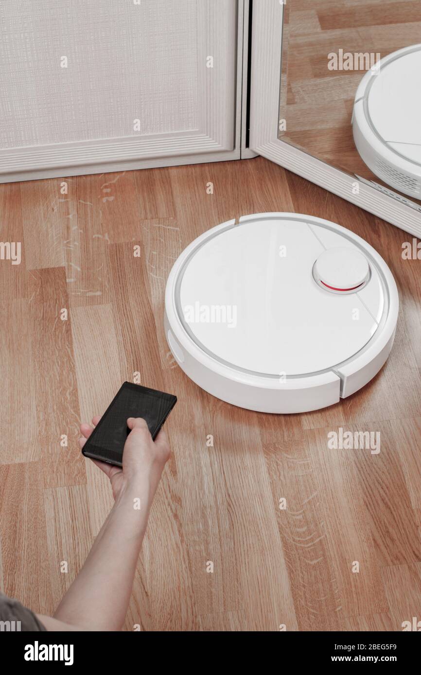 womens hand using mobile to control white robotic vacuum cleaner ...