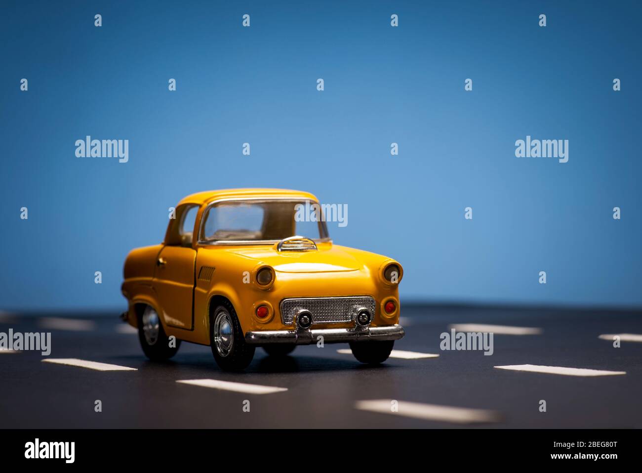 Front view of a Yellow toy car on a blue background and on an asphalt ...
