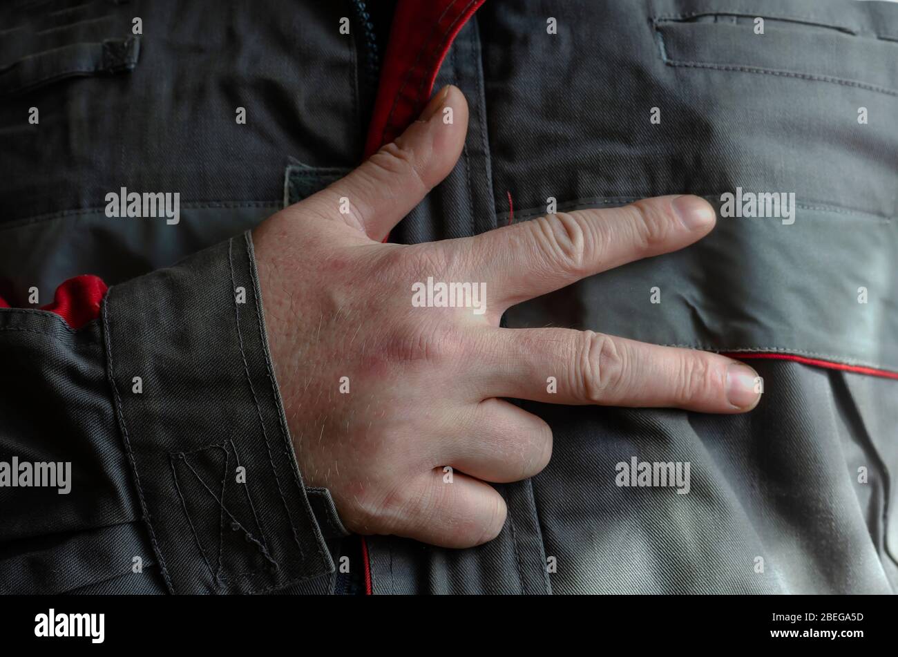 Man Shows Three Finger Gesture. A middle-aged man in work clothes shows ...