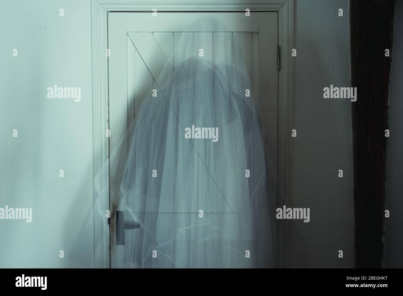 A spooky, transparent blurred ghost floating through a wooden door in a ...
