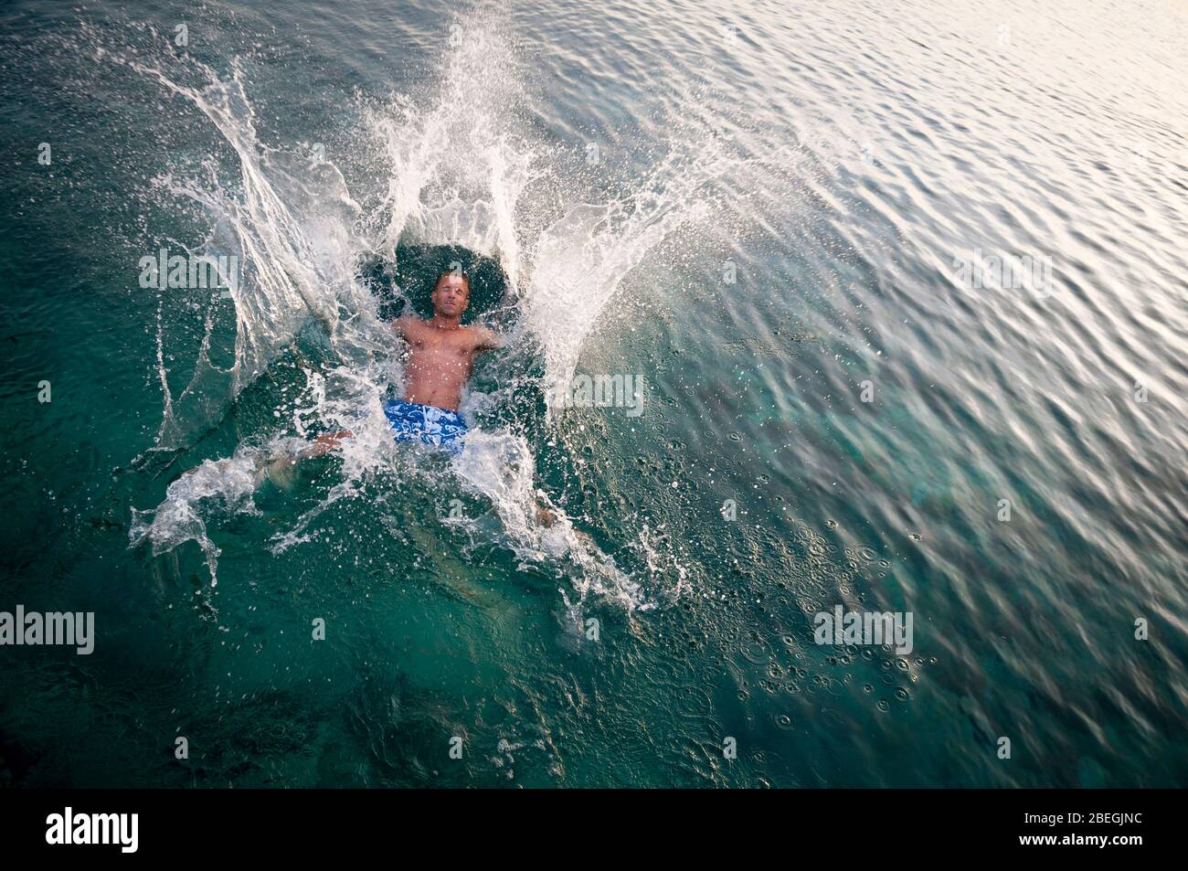 Action shot of man falling back into emerald water with a big splash ...