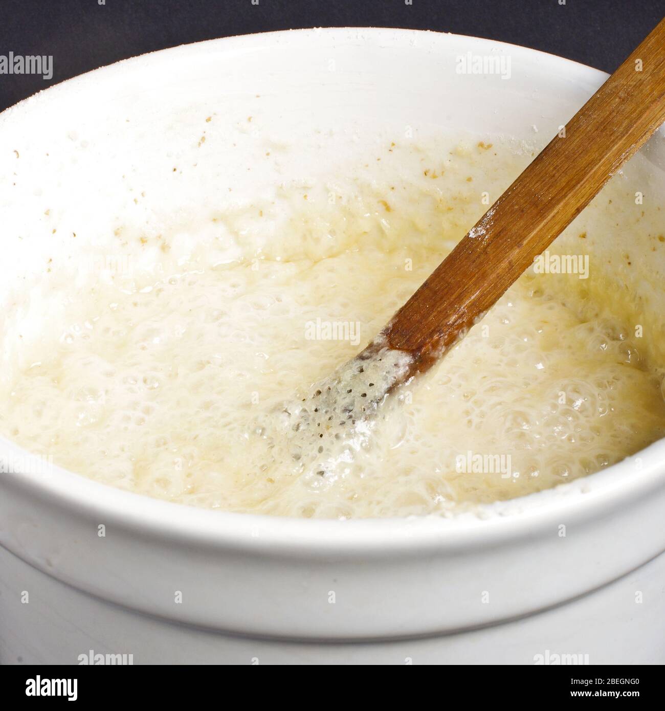 Mixing homemade bread dough in the white pot isolated on the black ...