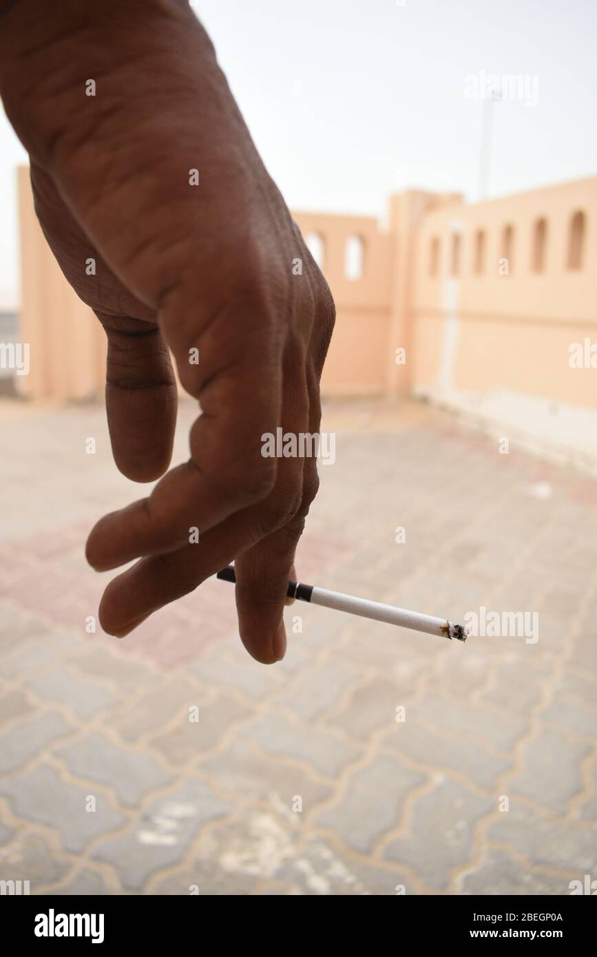 Closeup view of burning cigarette holding with two fingers and a wall ...