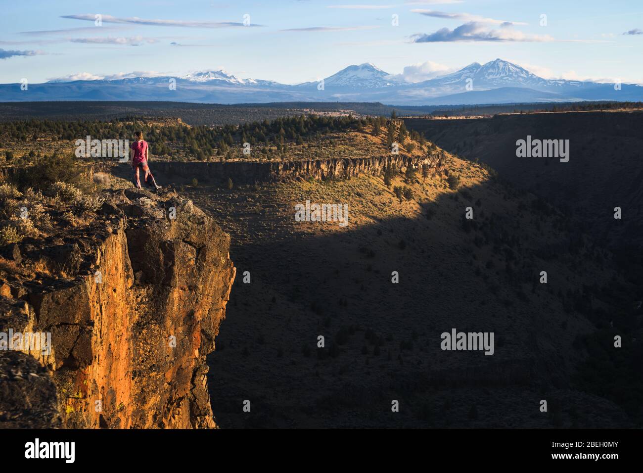 Woman standing on edge of cliff overlooking canyon and mountains Stock ...