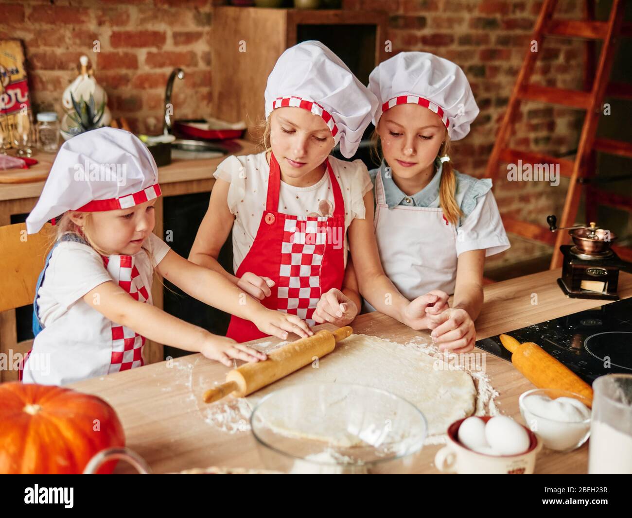 Three little chefs enjoying in the kitchen making cakes. Girls at the ...