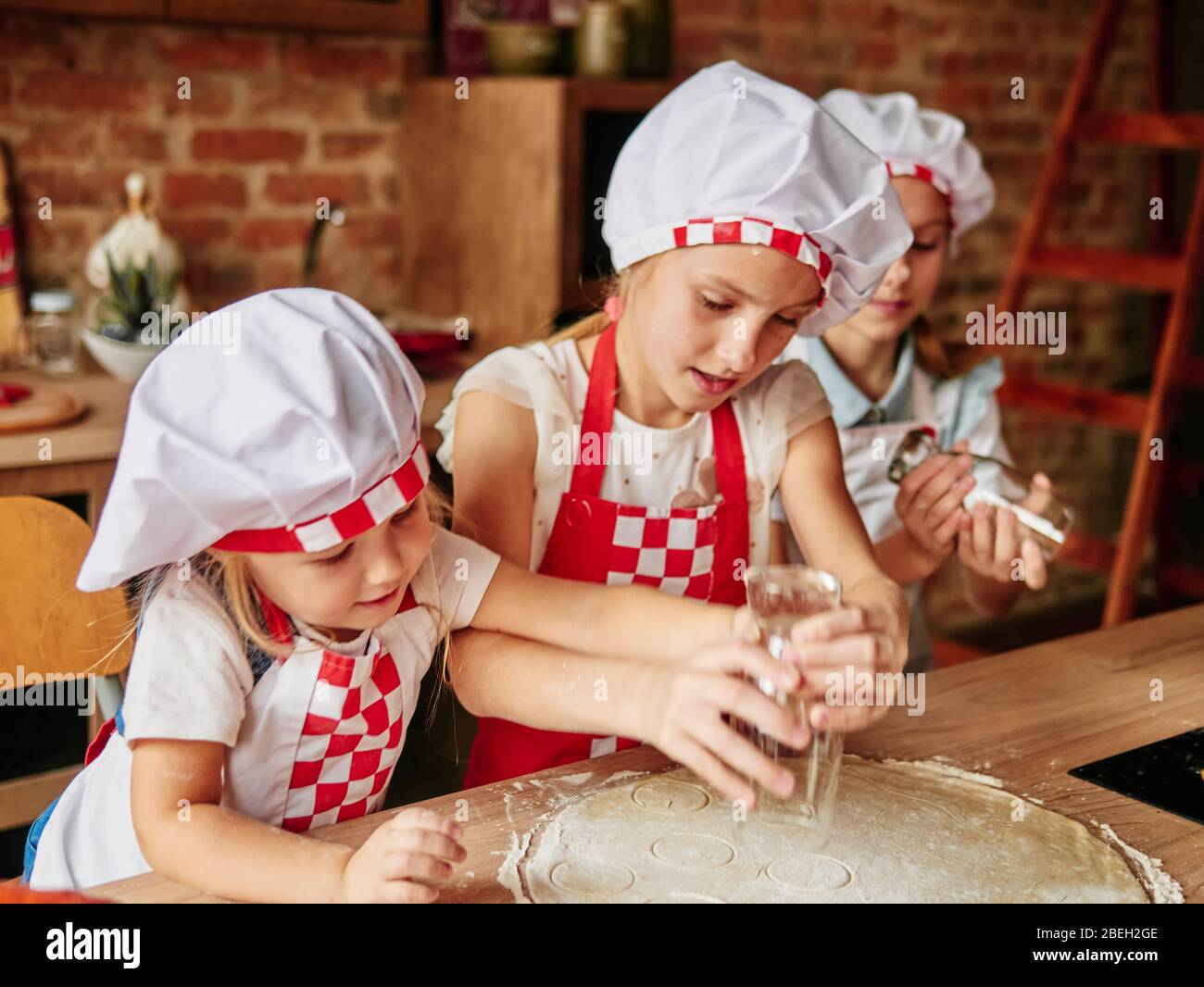 Three little chefs enjoying in the kitchen making cakes. Girls at the ...