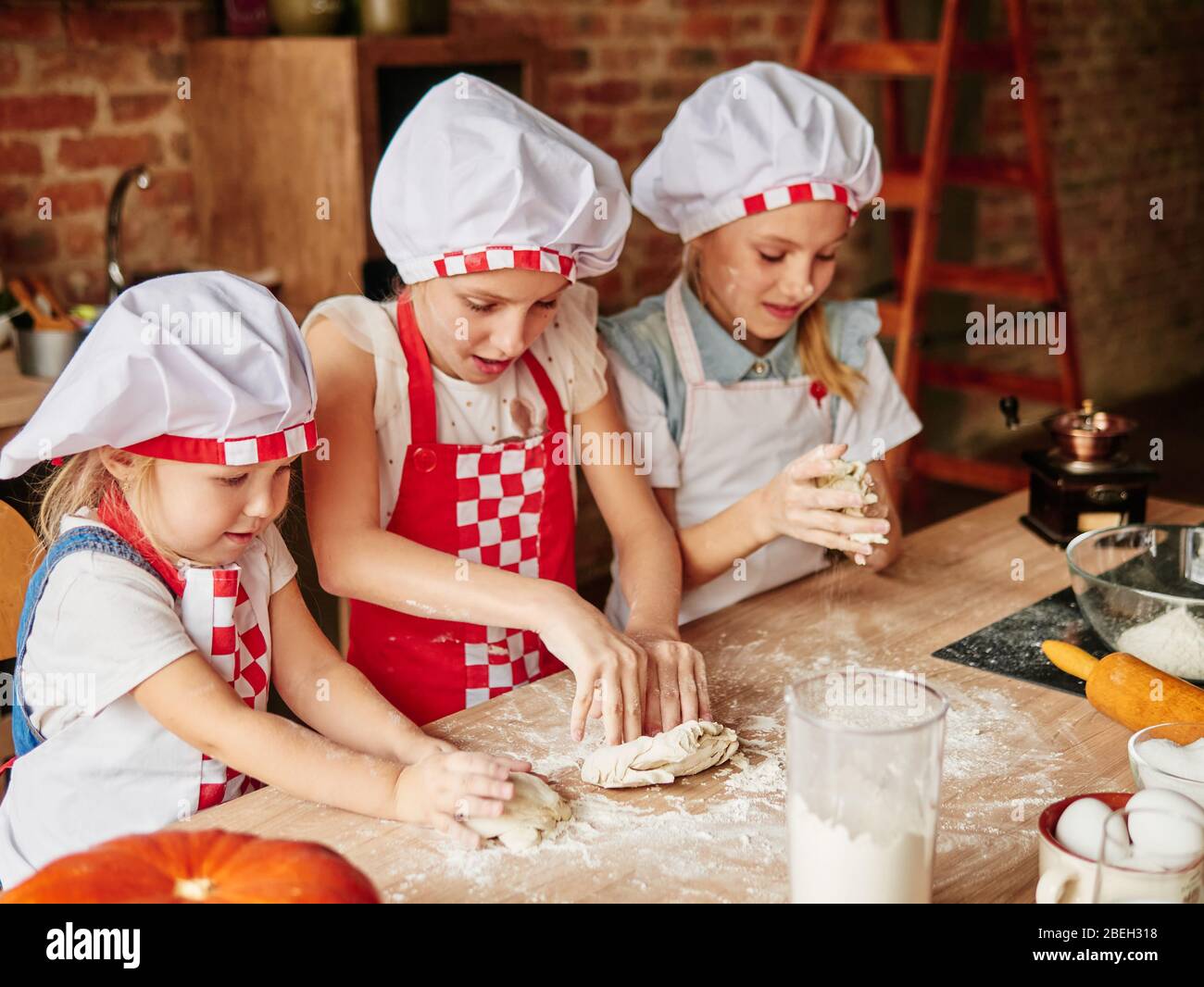 Three little chefs enjoying in the kitchen making cakes. Girls at the ...