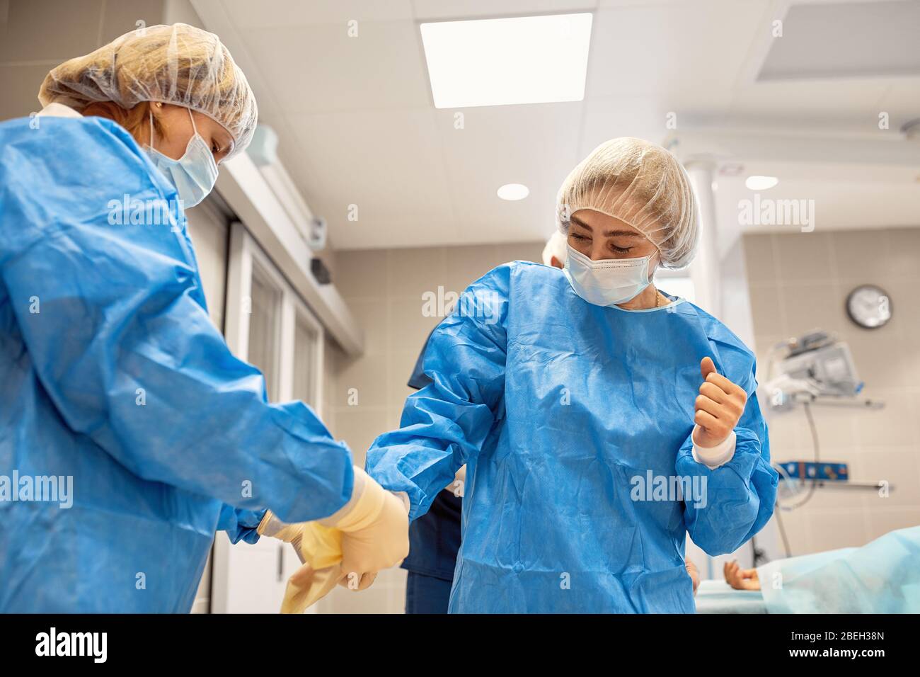 Operating room assistant helping the surgeon by putting on sterile ...