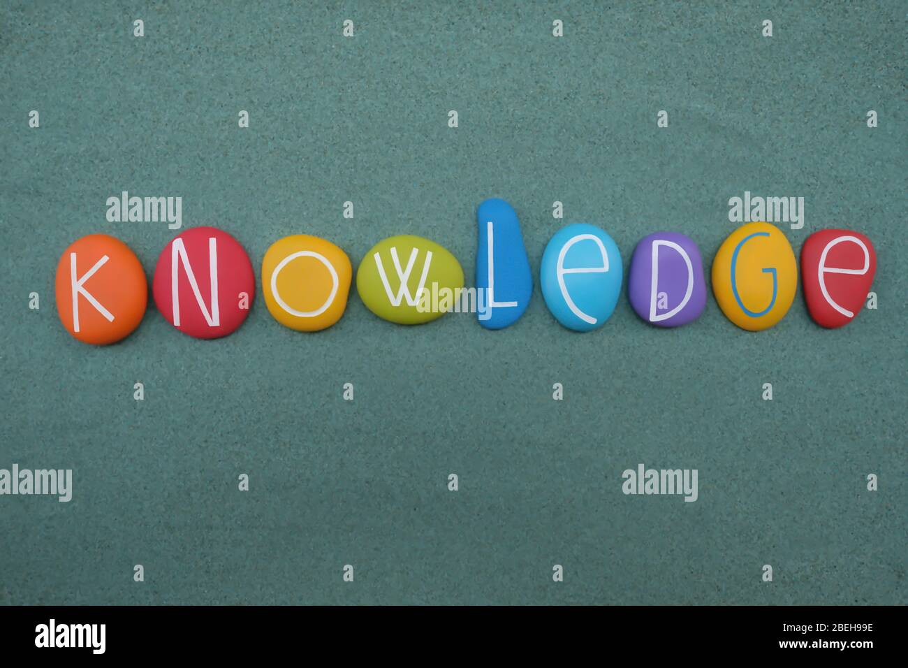 Knowledge word composed with multi colored stone letters over green ...