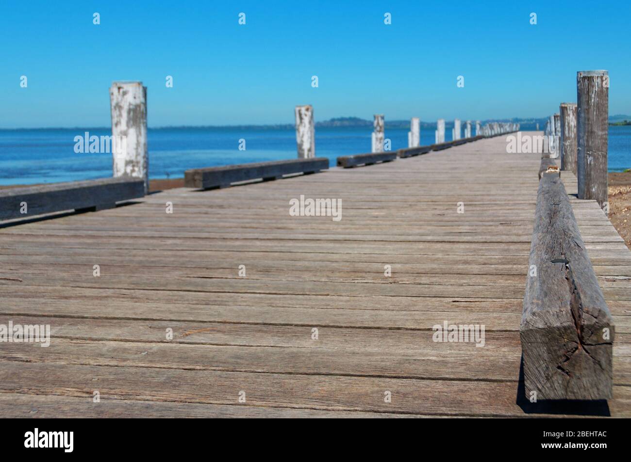 Long wooden jetty, pier with blue ocean and clear sky. Perspective view ...
