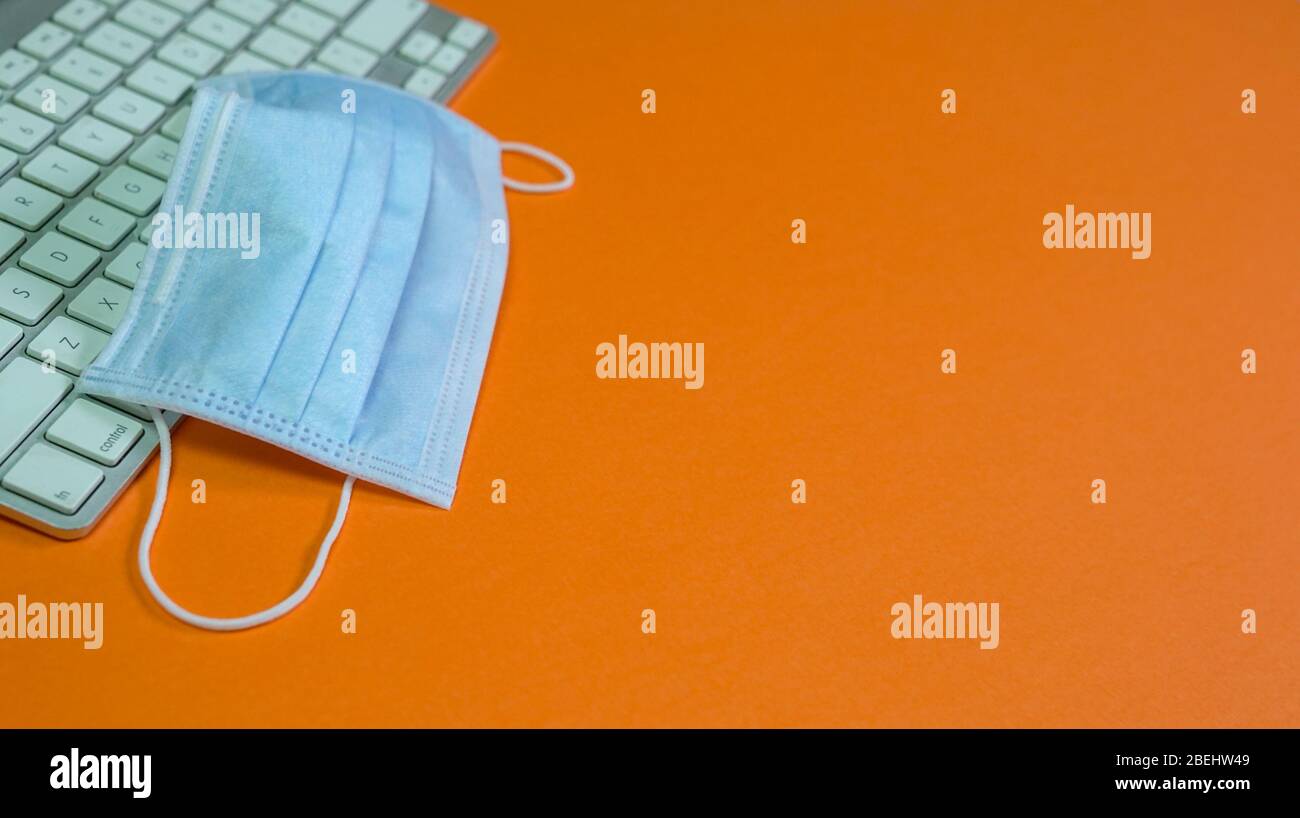 Medical face mask on top of keyboard. Orange background. Top view. Copy ...