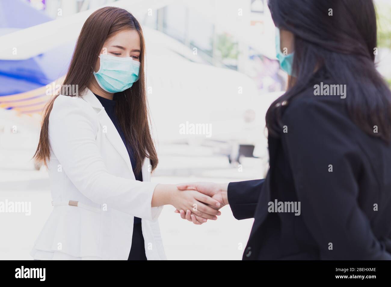 Two business woman wearing mask and making handshake in the city ...